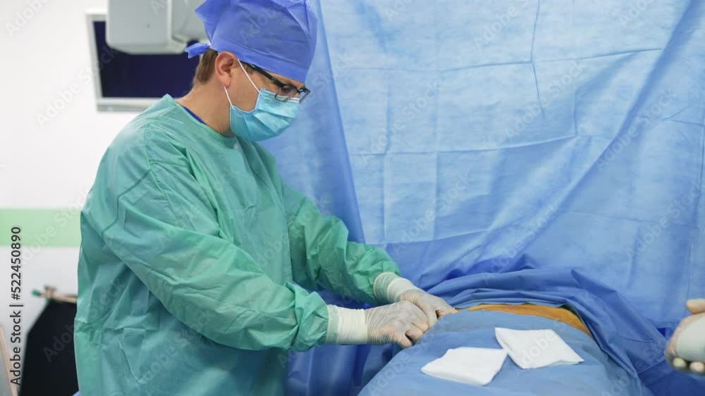 Doctor In Blue Robe Hat And Mask Stands At The Operational Table