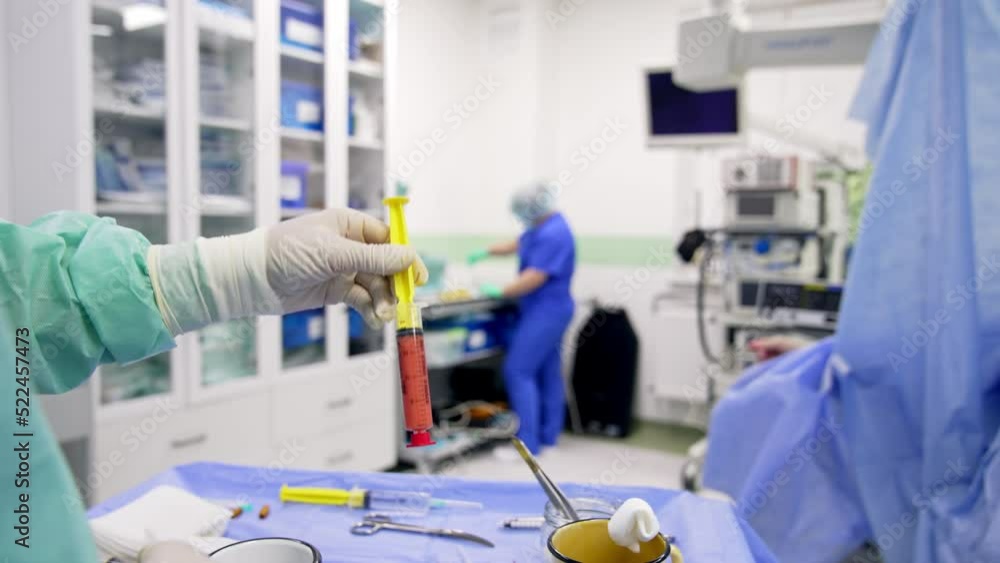 Doctor’s gloved hand puts a syringe with no needle on the table with ...