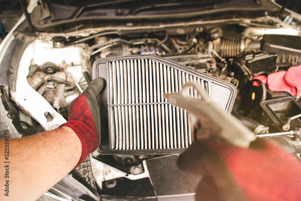 Car air filter in auto mechanic hand is blowing dust and cleaning with ...