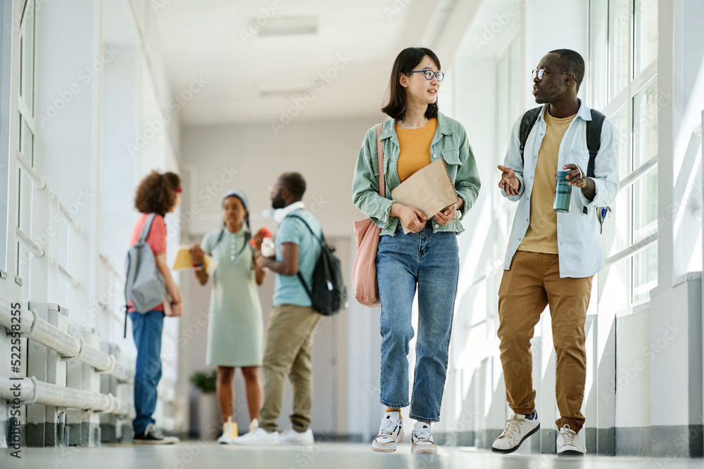 Classmates walking along school corridor and talking to each other ...