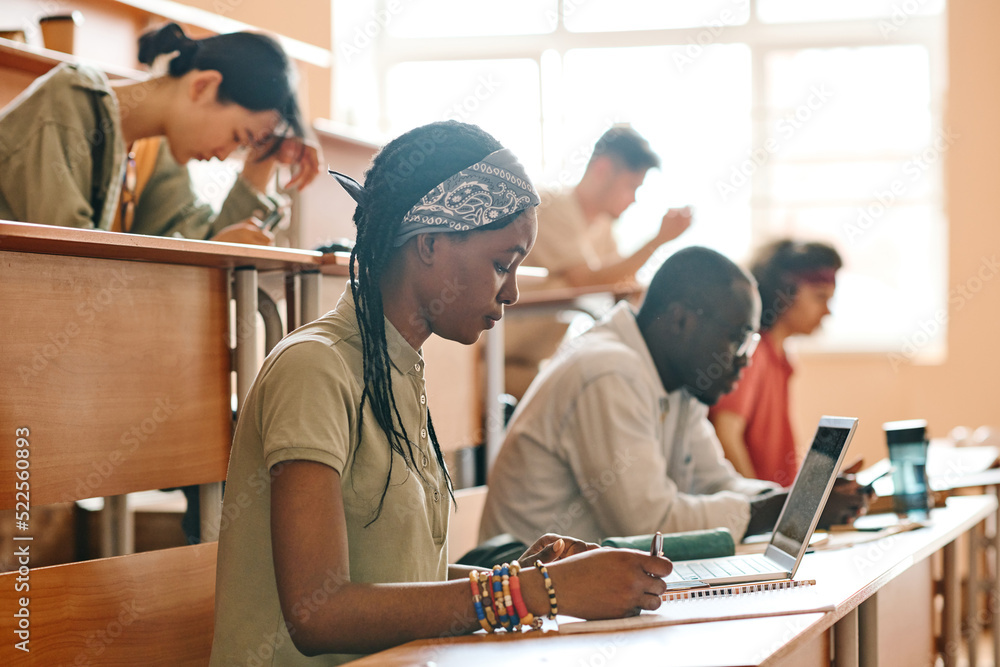 Group of students sitting at desk with laptop and books and writing ...