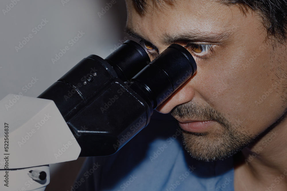 A brunette histologist doctor in a blue medical uniform looks in a ...