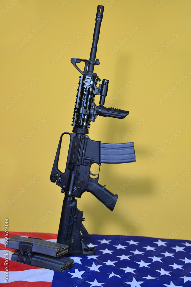 An American-made automatic carbine rifle standing over the US flag. A ...