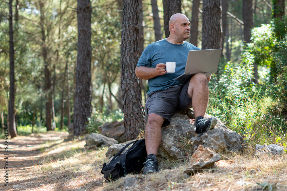 Digital nomad man enjoys working with a laptop sitting on a rock in a ...