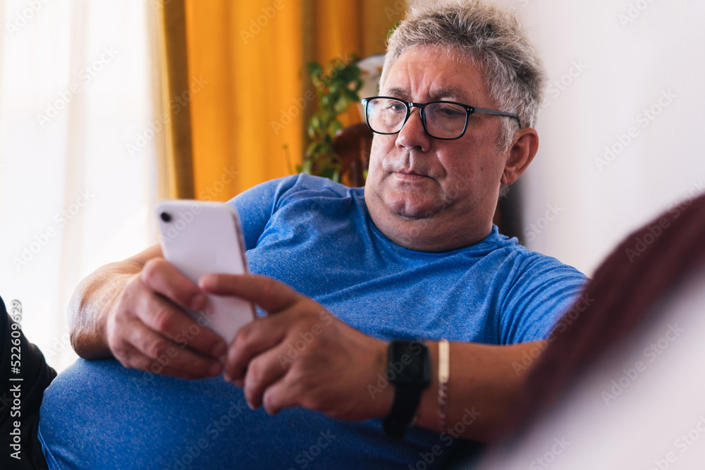 Elderly man with gray hair lying on his side on his sofa using his ...