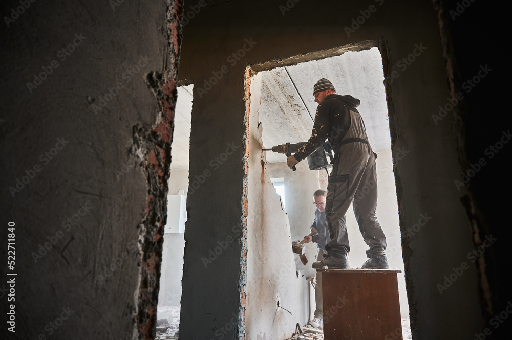 Bottom view of two builders deconstructing interior partition. One ...