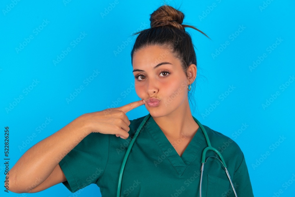 Charming beautiful doctor woman wearing medical uniform over blue ...