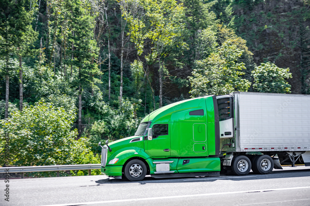 Bright green industrial big rig semi truck transporting cargo in ...