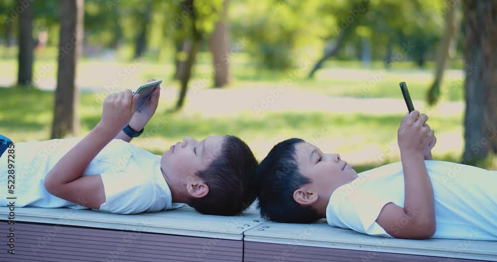 Two boys play on smartphones during an outdoor walk. They are lying on ...