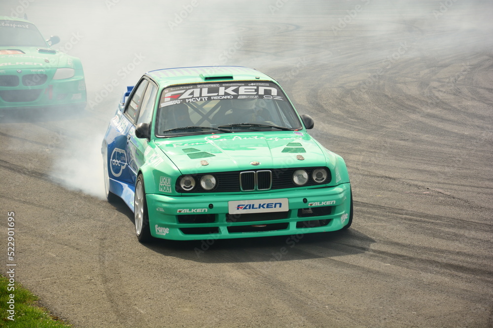 Oldtimer BMW e30 M3 im Falken-Design driftet um Pylonen bei einer ...