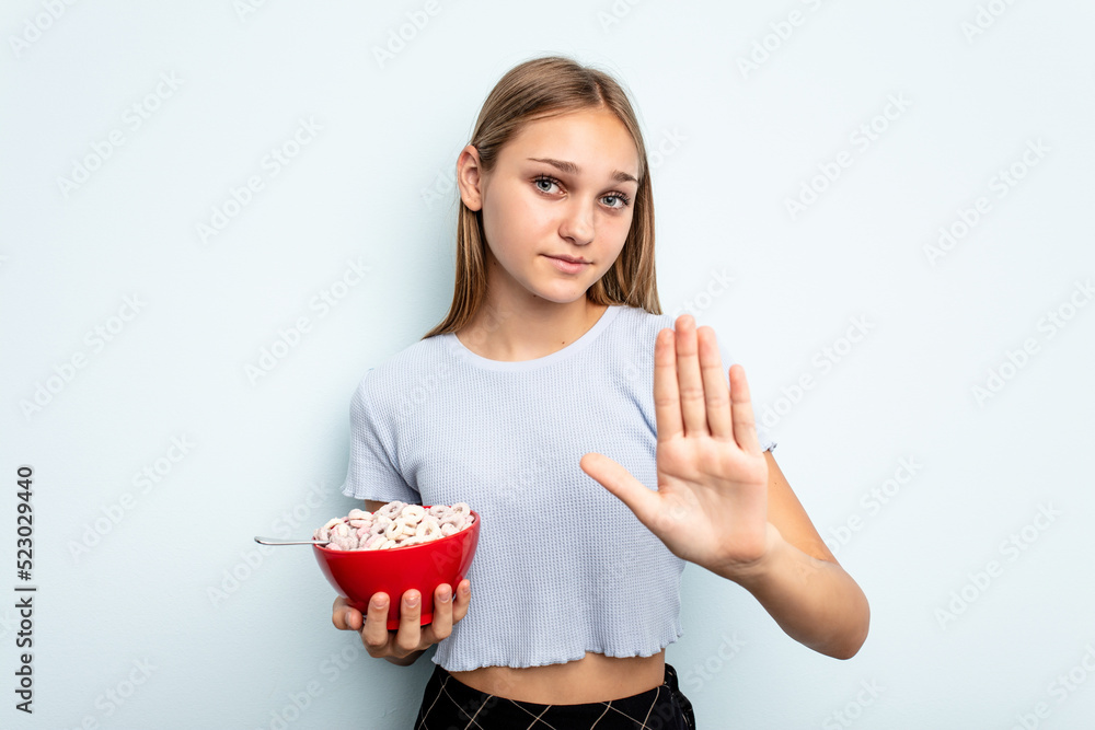Young caucasian girl eating cereals isolated on blue background ...