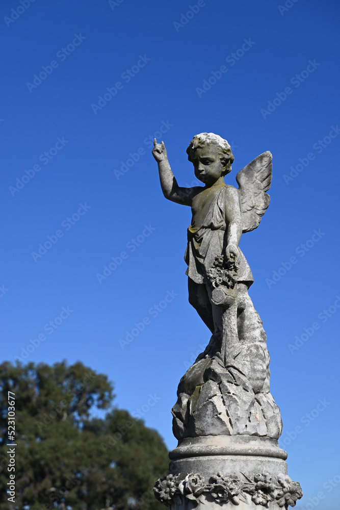 Stone sculpture of a child angel, or cherub, pointing skyward whilst ...