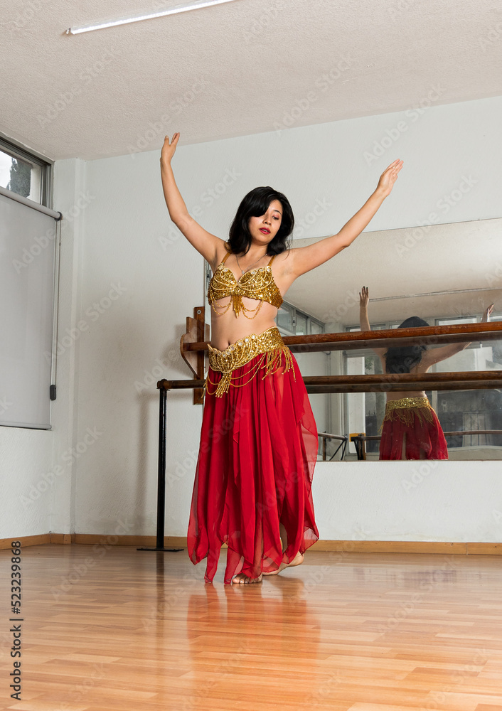 young bellydancer dressed in a red and gold costume practicing in a ...