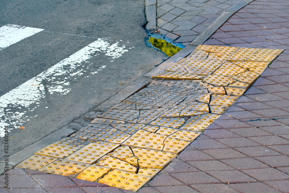 Cracked yellow tactile tiles on asphalt road in front of pedestrian ...