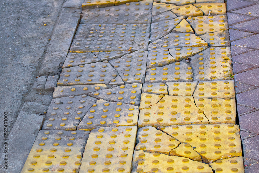Damaged and dirty yellow tactile tiles on asphalt road. Damaged warning ...