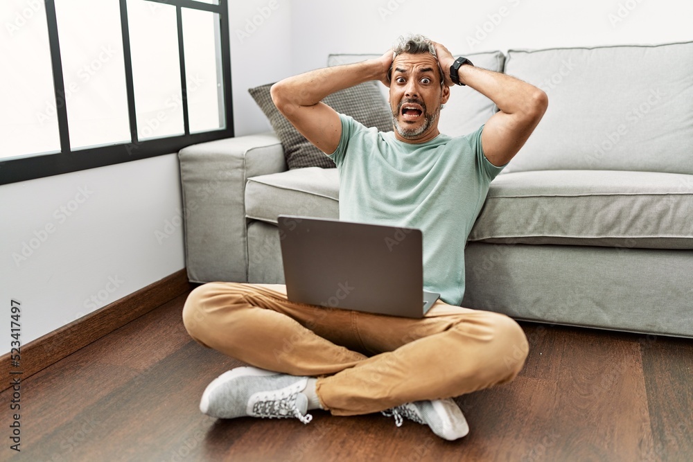 Middle age hispanic man using laptop sitting on the floor at the living ...
