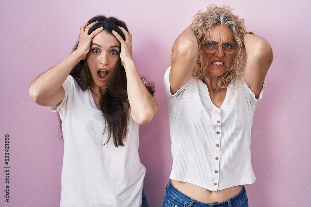 Mother and daughter standing together over pink background crazy and ...