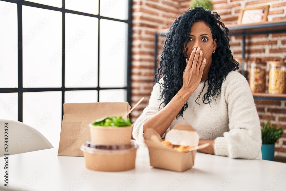 Middle age hispanic woman eating take away food covering mouth with ...
