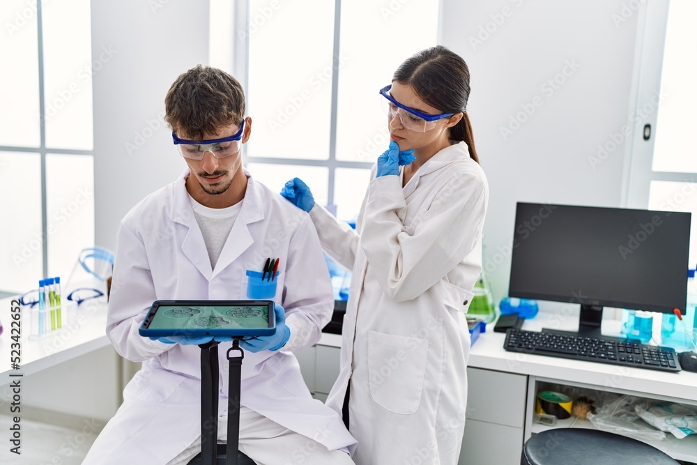 Man and woman partners wearing scientist uniform using touchpad with ...