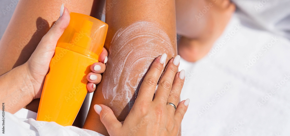 Sun protection cream for skin care. Close-up of a woman's legs applying ...