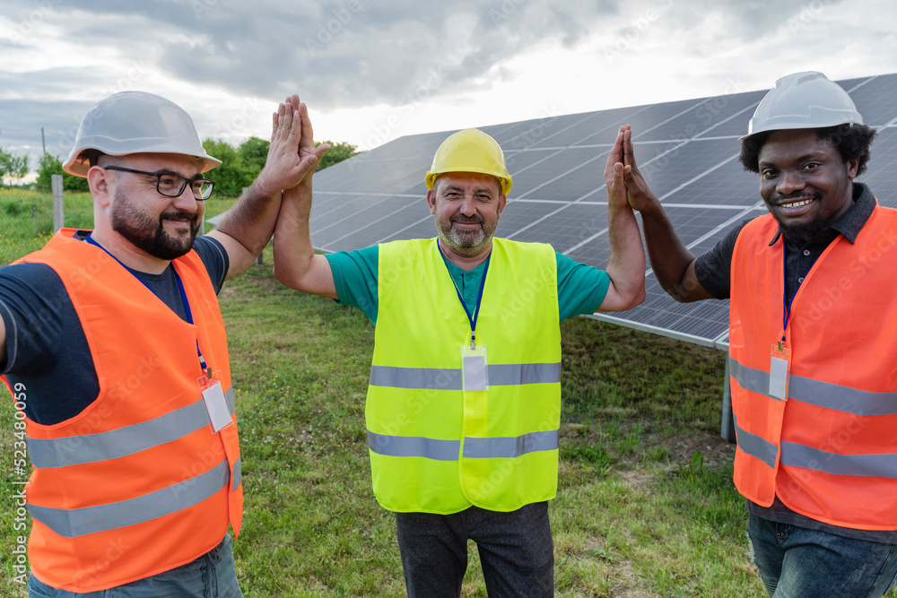 Smiling engineers giving high five to each other at solar power station ...