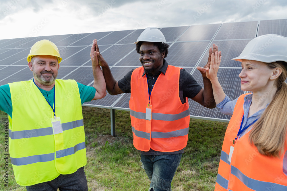 Smiling multiracial engineers giving high five to each other at solar ...