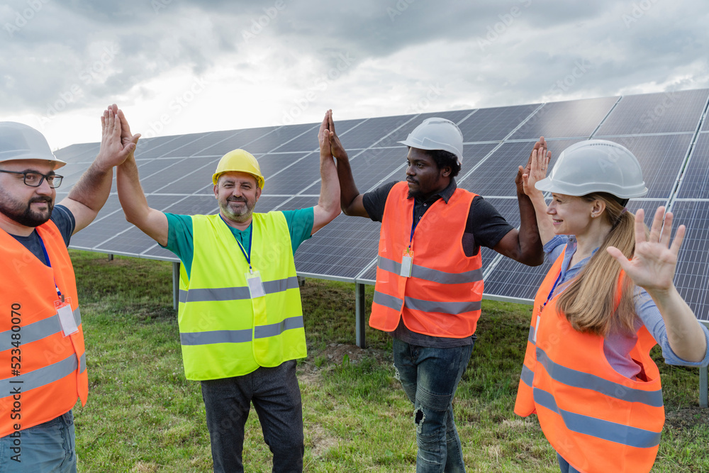 Smiling engineers high-fiving and standing in front of solar panels at ...