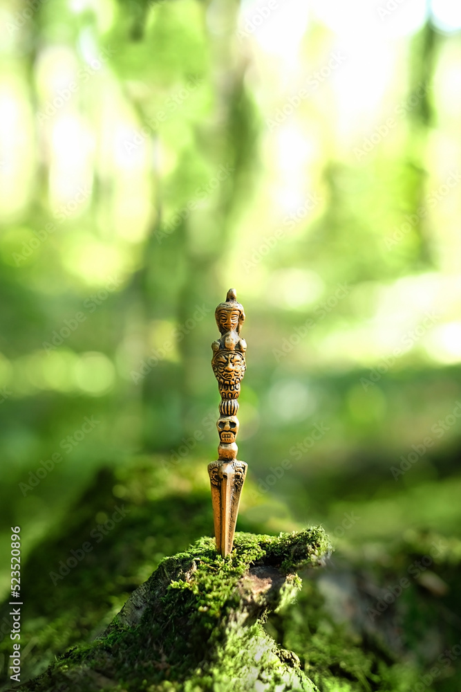 Ritual knife on mossy stump, blurred natural green background. Phurba ...