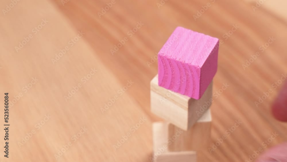 Stacking a pink toy cube on top of a pyramid of wooden blocks ...