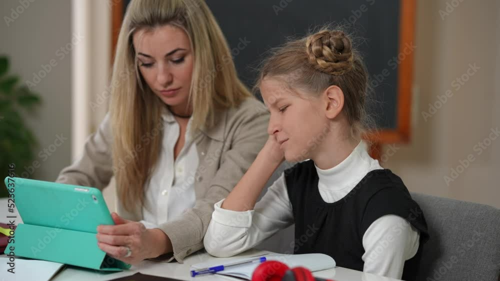 Side view tired teenage girl sitting with teacher at desk talking ...
