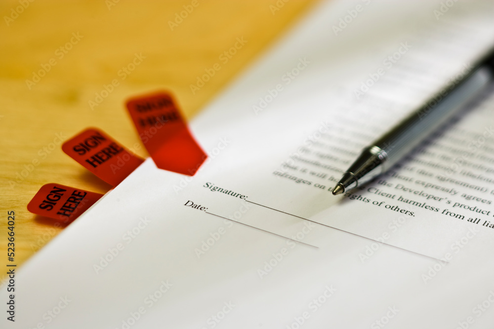 Documents requiring signature with pen and sign here tabs on a desk ...