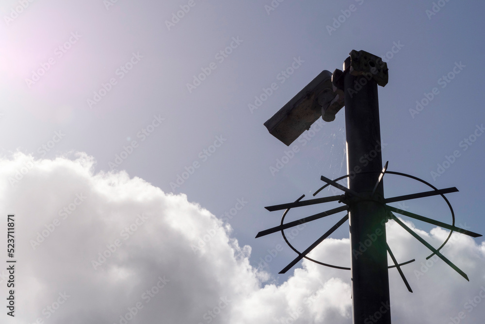 Silhouette of a security camera mounted on a tall pole against sunny ...