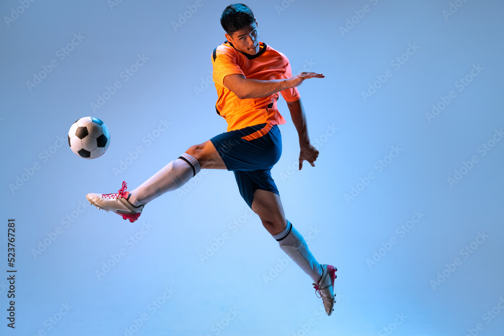 Portrait of young man in uniform, professional football player kicking ...