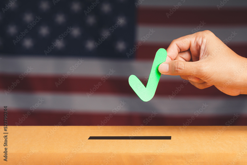 Hand holding a green check mark symbol overhead the voting box at place ...