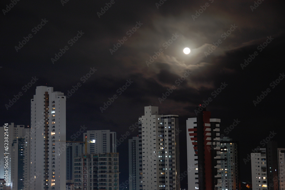 Noite de lua cheia parcialmente nublado entre prédios em rotatória de ...