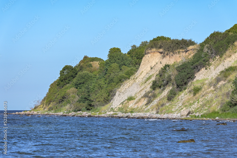 Steep coast with shrub vegetation and erosion of clay and boulders in a ...