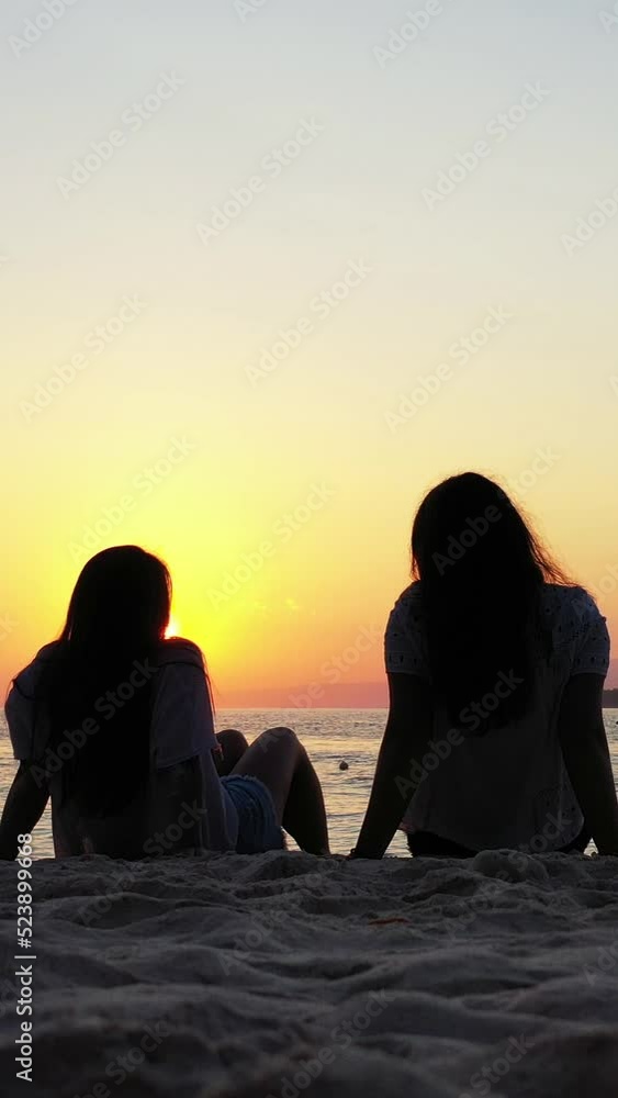 Vertical footage of two young girls sitting on the beach together and ...