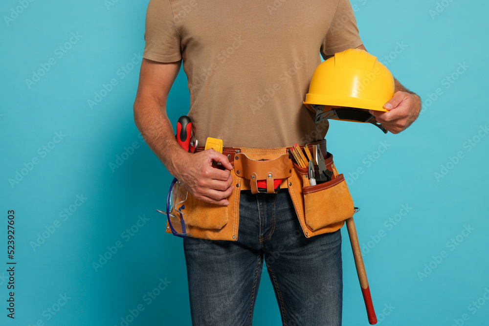 Professional builder with hard hat and tool belt on light blue ...