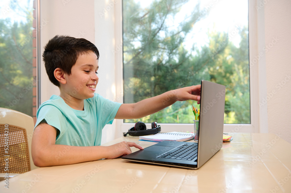 Handsome judicious smart schoolboy sits at the laptop, preparing for an ...