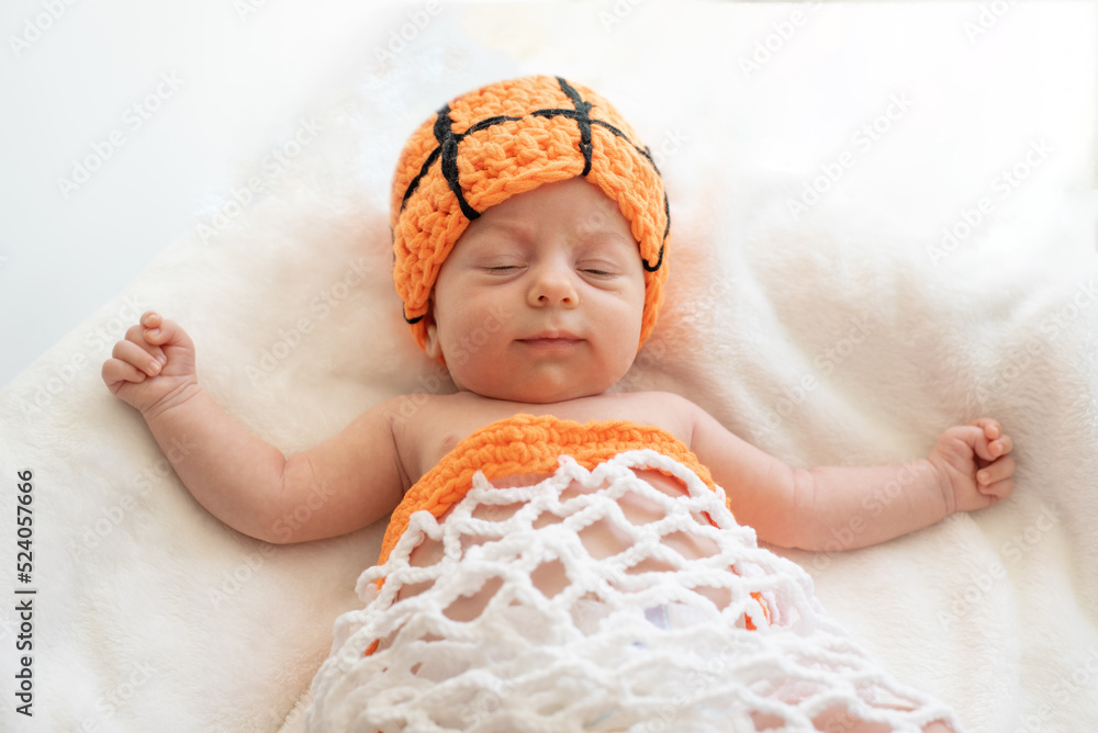 Newborn baby sleeping on his back on white blanket with orange hat as ...
