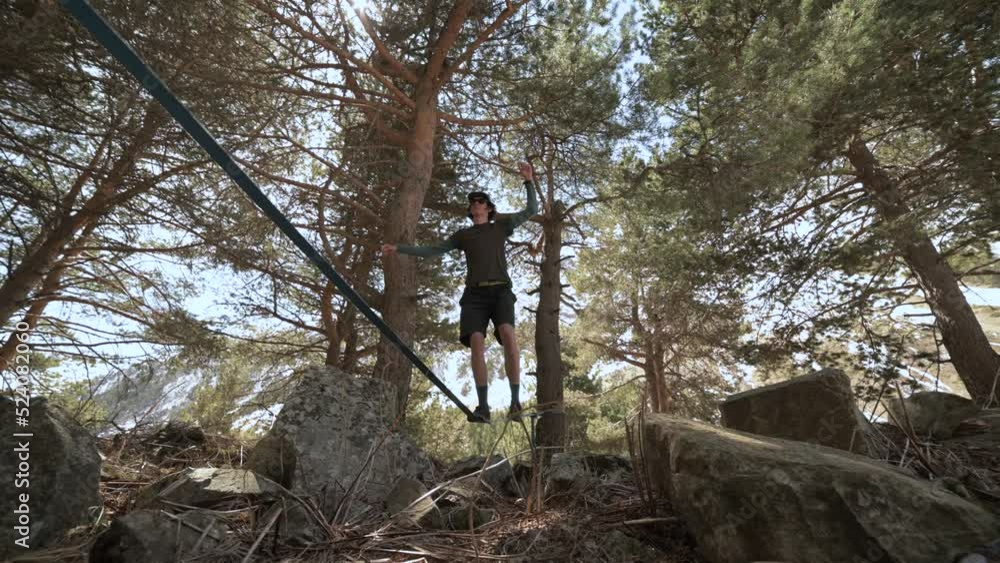 A young man walks on a slackline and balances on a rope bright sunlight ...