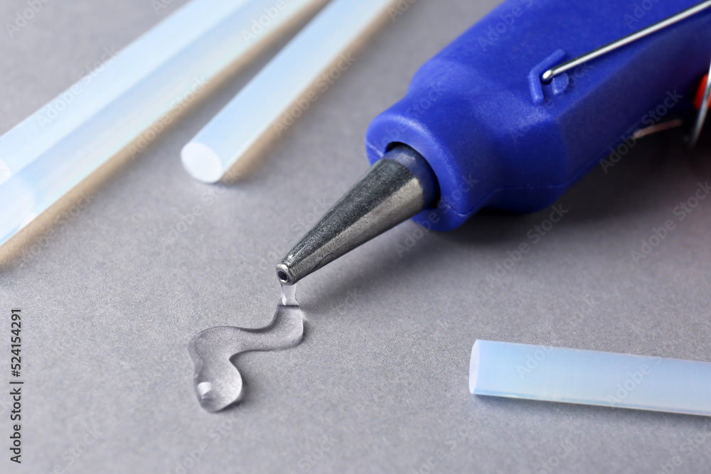Melted glue dripping out of hot gun nozzle near sticks on grey ...
