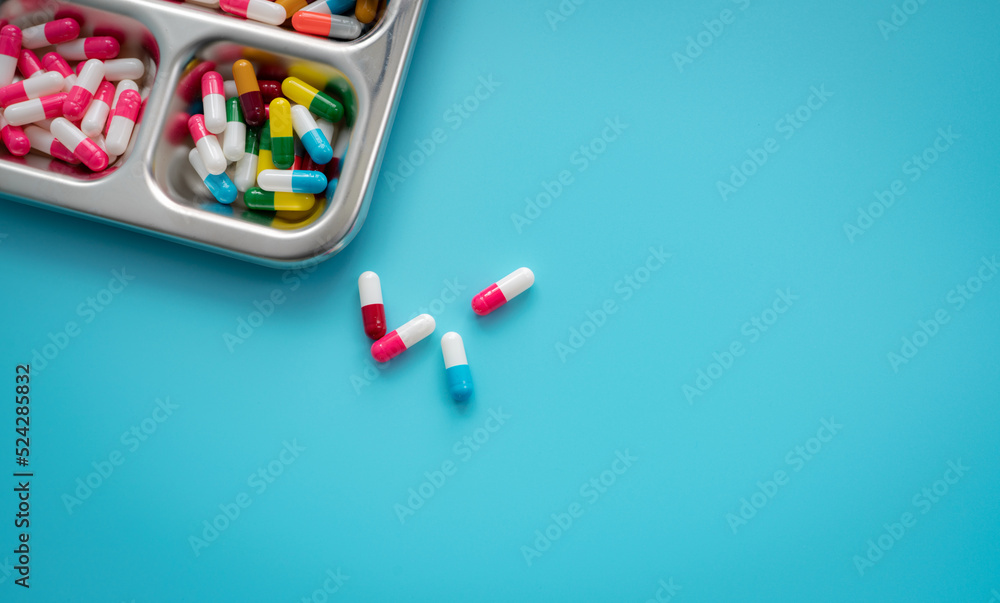 Multi-colored capsule pills in stainless steel tray and on blue ...