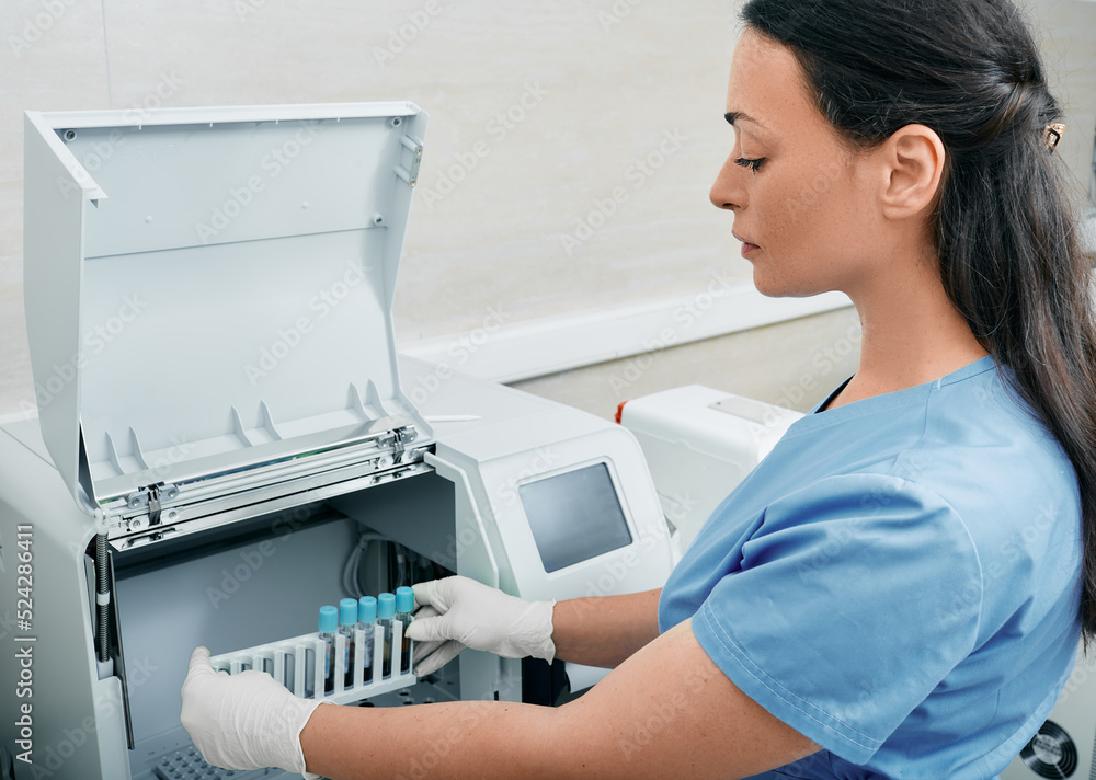 Blood sample coagulation analysis. Female laboratory technician loading ...