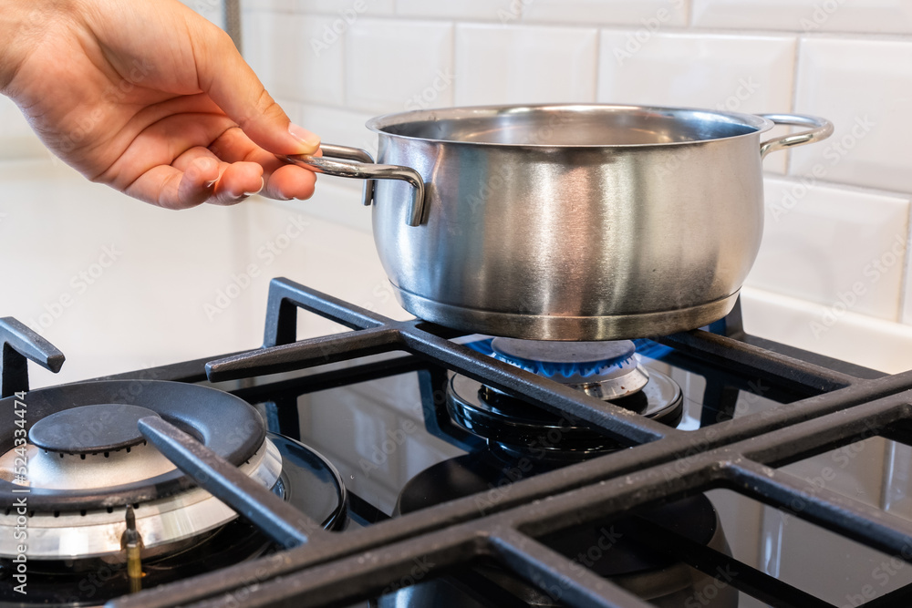 Female hand holding saucepan standing on the gas burner of the stove ...