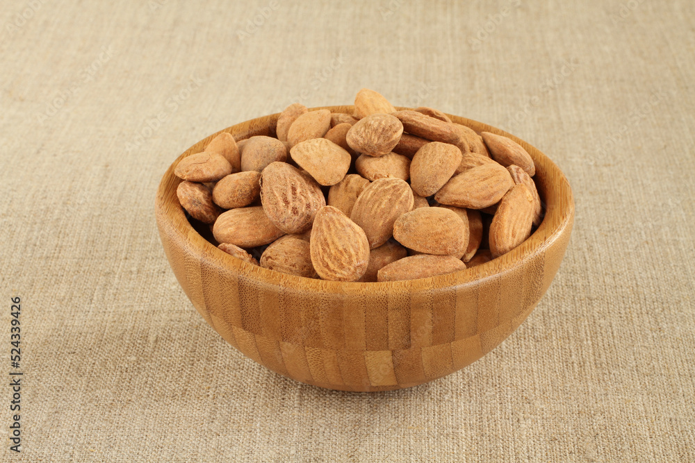 Big shelled roasted salted almonds in bamboo bowl on rough linen cloth ...