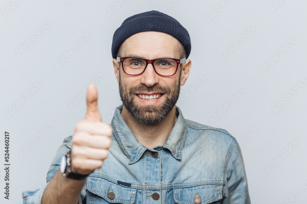 Positive middle aged male with thick beard and mustache, shows ok sign, raises thumb, dressed in ...