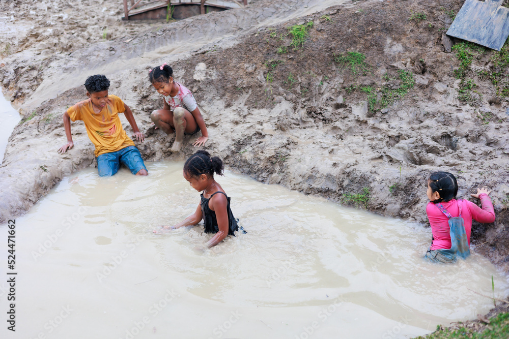 African child and asian girl playing in puddle mud together at outdoor ...