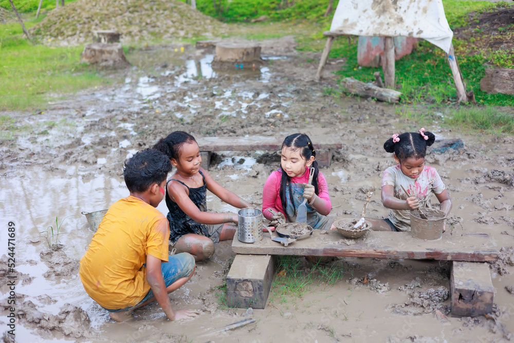Foto de African child and asian girl playing in puddle mud together at ...