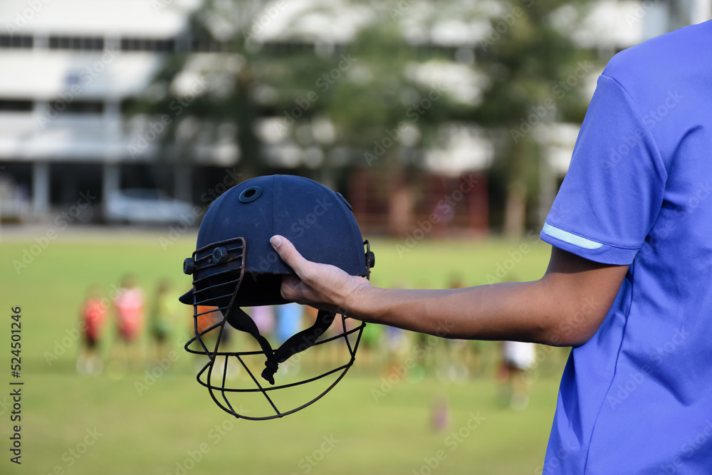 Cricket helmet holding in hand of cricketer, blurred green grass ...